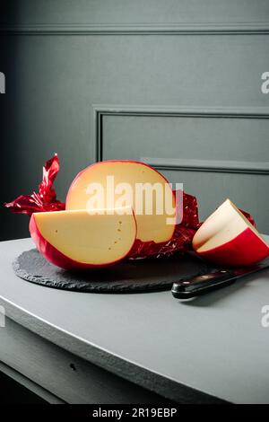 head of Edam cheese with a red crust lying on a brouwn wooden table ...