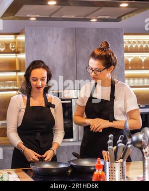 Two funny professional female chefs preparing food in large kitchen and ...