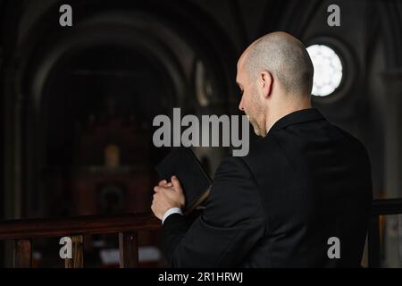 Mature pastor in black suit speaking prayer in microphone while ...