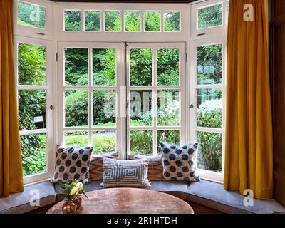 Wooden table near bay window seat with cushions in cozy room. Interior ...