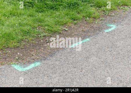 Green spray-painted markings on tarmac surfaced small road. For UK road ...