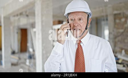 Senior grey-haired architect man holding blueprints using smartphone at ...