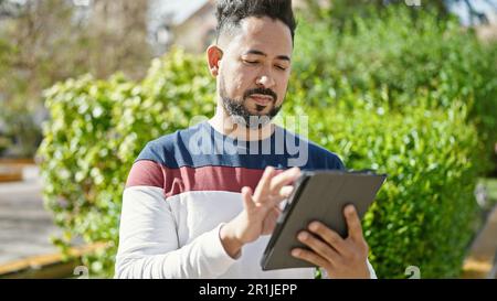 Hispanic man with beard using touchpad sitting on the sofa smiling ...