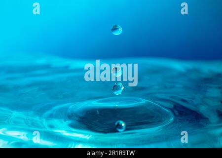 Water droplets fall down closely into the blue water, making it the ...