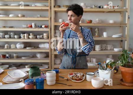 Young woman potter resting in cozy home pottery studio, drinking tea ...