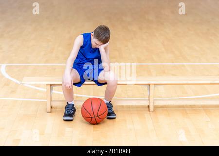 Sad disappointed boy with basketball ball in a physical education ...