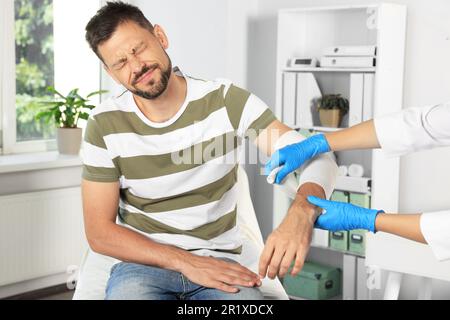 Doctor applying bandage onto patient's arm on white background, closeup ...