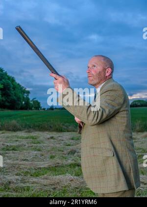 An English gentleman stood at twilight in a tweed shooting suit with a ...