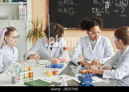 Diverse group of schoolchildren wearing lab coats during science ...