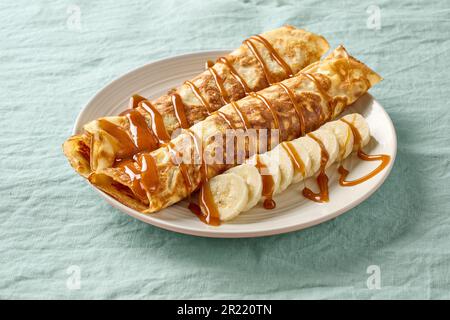 freshly baked crepes with banana and melted caramel sauce on plate ...