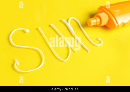 Bottle with sunscreen and word SUN made of cream on yellow background ...