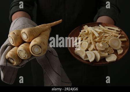 Woman holding whole and cut parsnips on black background, closeup Stock ...