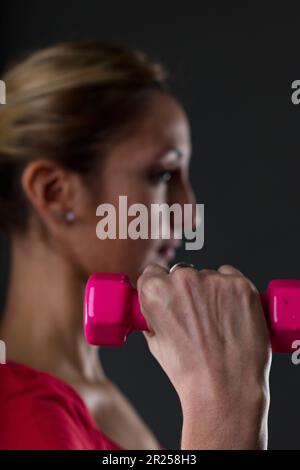 Woman lifting pink dumbbell, blurred background. Blonde, red top ...
