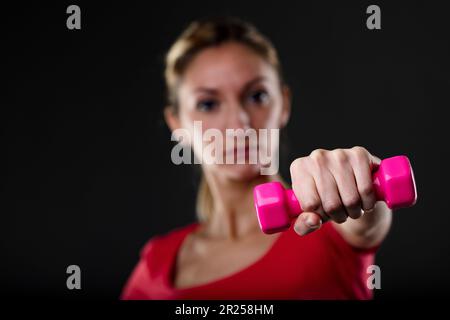 Woman lifting pink dumbbell, blurred background. Blonde, red top ...