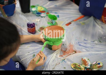 Little kid colouring a pot with messy green colo. A kid holding a pot ...