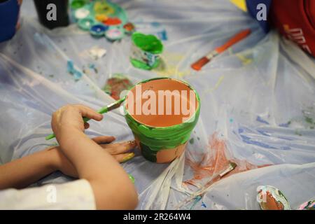 Little kid colouring a pot with messy green colo. A kid holding a pot ...