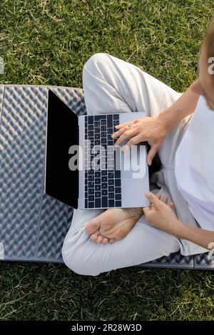 Cropped view of a yogi sitting on a fitness mat, meditating with rosary ...