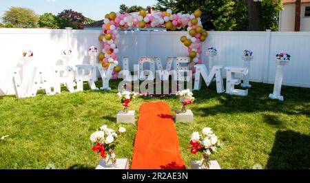 A backyard is set up for a marriage proposal with a red carpet leading ...