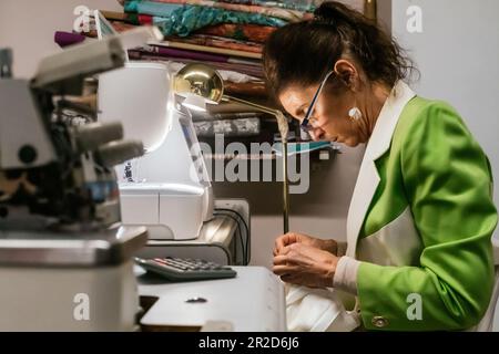 Adult dressmaker woman sews clothes on sewing machine. Happy seamstress ...