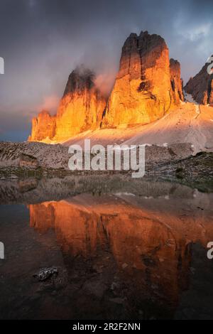 Dramatic Alpine glow of the Three Peaks with reflection in mountain ...