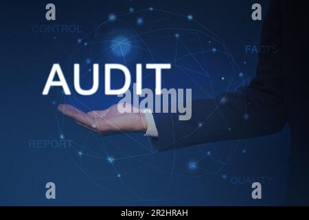 Audit concept. Businessman holding digital word in hand on dark ...