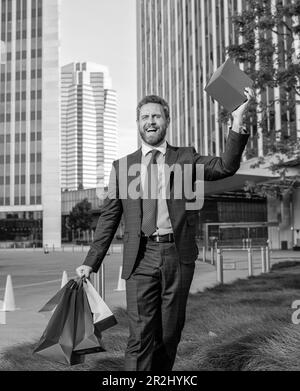laughing man in formalwear with shopping bags and present box walk ...