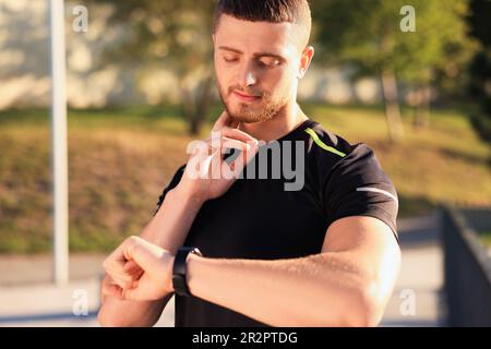 Attractive serious man checking pulse after training on stairs in park ...