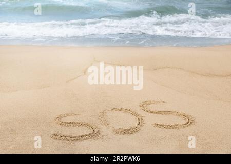 Message SOS drawn on sand near sea Stock Photo - Alamy