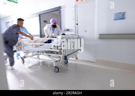 Diverse doctors urgently pushing patient lying in bed in corridor at ...