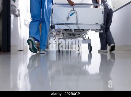 Low section of diverse doctors pushing patient in hospital bed down ...