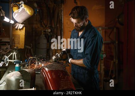Repairman grinding motorcycle body part from old paint using stripping ...