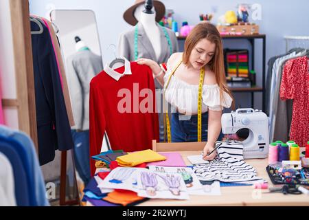 Young redhead woman tailor holding t shirt at clothing factory Stock ...