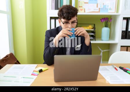 Non binary man business worker using laptop drinking coffee at office ...