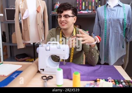 Non binary man tailor smiling confident sitting on table at atelier ...