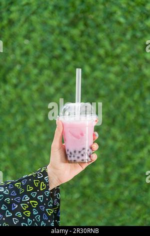Woman holding bubble tea with lemonade in front of gray stone wall ...