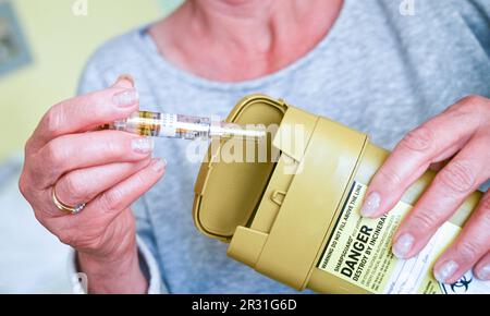 Woman disposing of a used needle in a Sharpsguard disposal waste unit ...
