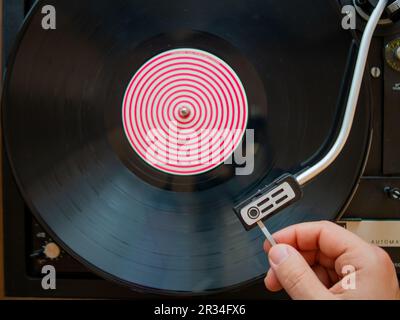 Detail of a male hand placing the needle on the track of a red vinyl ...