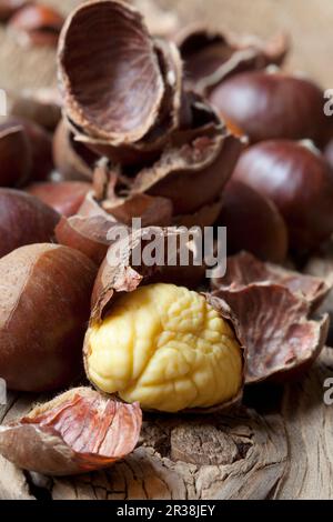 Roasted chestnuts, one peeled, on a dark wooden background, vertical ...