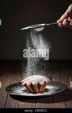 Man's hand sprinkling sugar over puff pastry sweets and angel hair in a ...