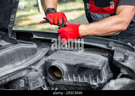 An auto mechanic opens the air filter housing of an internal combustion ...