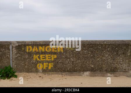 Seawall with warning sign painted onto the wall Stock Photo - Alamy