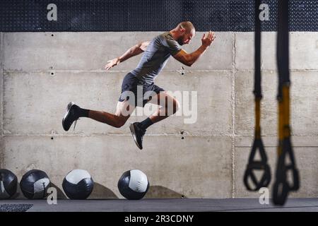 A muscular man captured in air as he jumps in a modern gym, showcasing ...