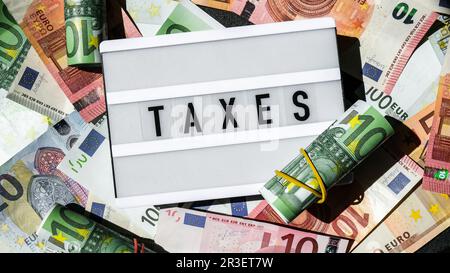 Lightbox board with word TAXES in black letters around Euro banknotes ...