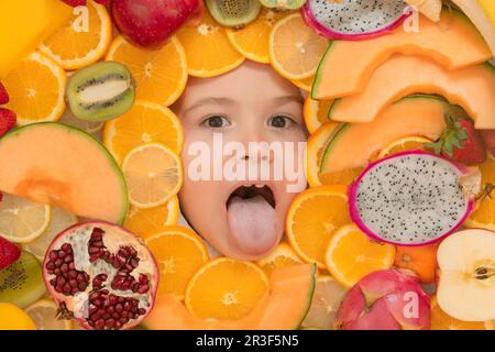 Funny licking fruit. Kid smiling face portrait surrounded by fruits ...