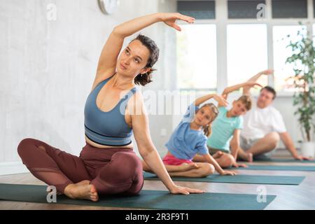 Teen girl doing Padmasana with side stretch during yoga workout in gym ...