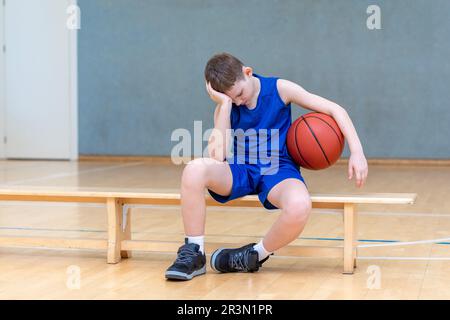 Sad disappointed boy with basketball ball in a physical education ...