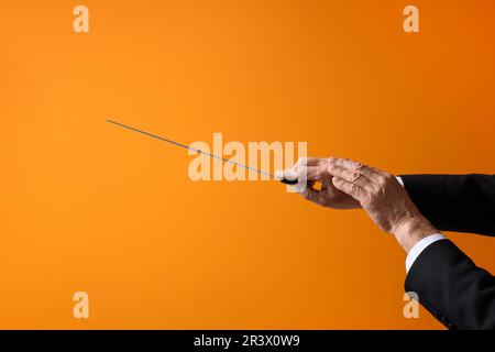 Professional conductor with baton on orange background, closeup. Space ...
