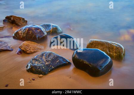 Multiple colors of smooth stones washed up on sandy shore Stock Photo ...