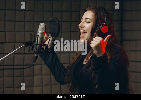 Female with microphone recording a voice for dubbing in music studio ...