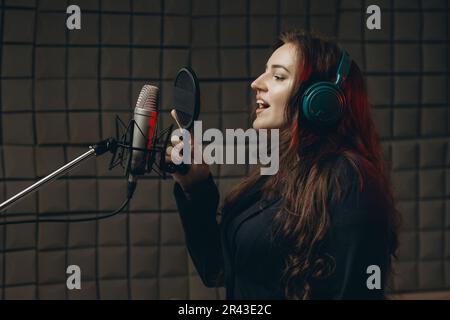 Female with microphone recording a voice for dubbing in music studio ...